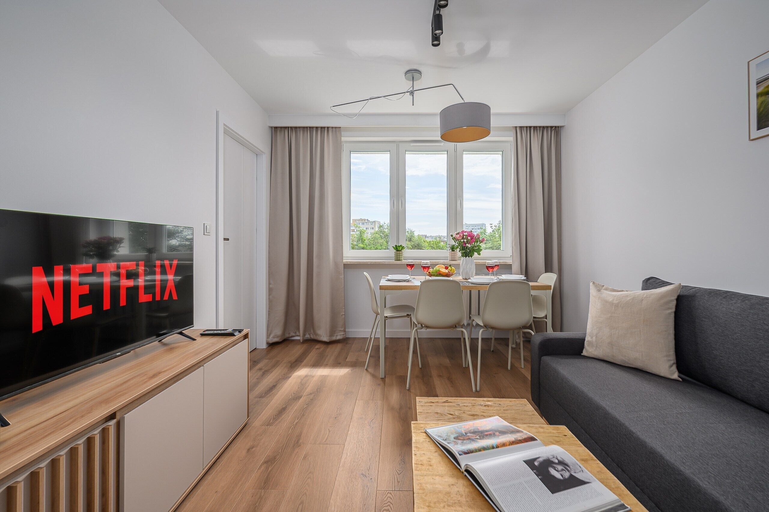 Uma sala de estar moderna com televisão de tela plana, sofá, área de jantar e vista para a cidade.