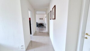 Um corredor com paredes brancas, chão de azulejos e uma porta à direita.