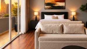 Quarto de hotel moderno com uma cama grande, duas mesas de cabeceira com abajures, vista para a cidade e um aparelho de ar condicionado na parede.