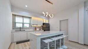 Uma cozinha moderna com armários brancos, uma ilha de mármore e banquetas.