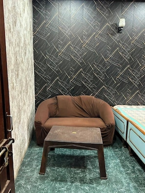 Um quarto com um sofá marrom, uma mesa de madeira pequena e uma cama com cabeceira estampada.