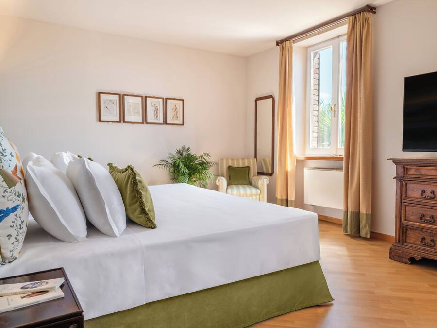 Quarto de hotel com cama, televisão, cômoda, cadeira e quadros na parede.