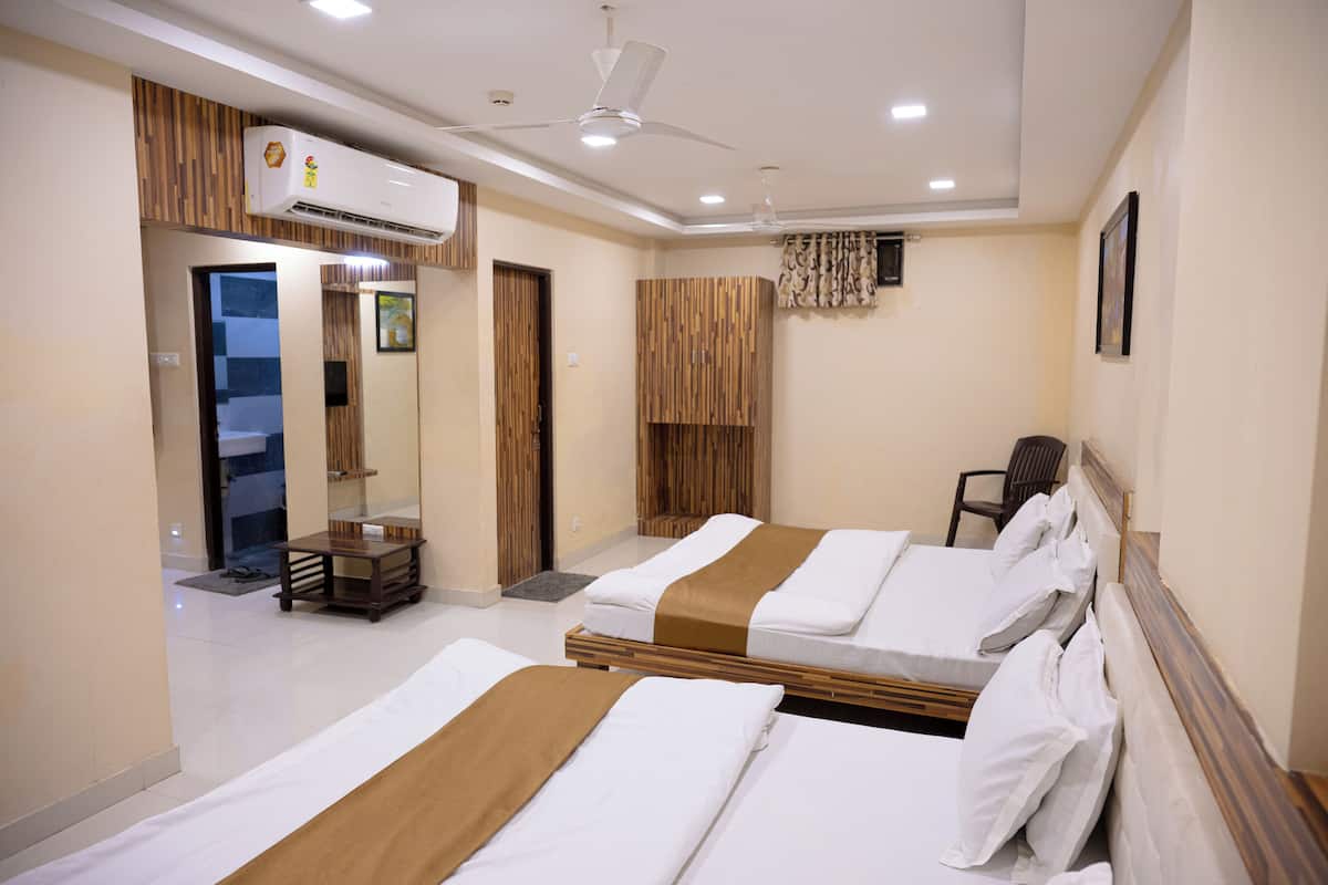 Quarto de hotel com duas camas, um ventilador de teto, aparelho de ar condicionado, guarda-roupa de madeira e uma cadeira.