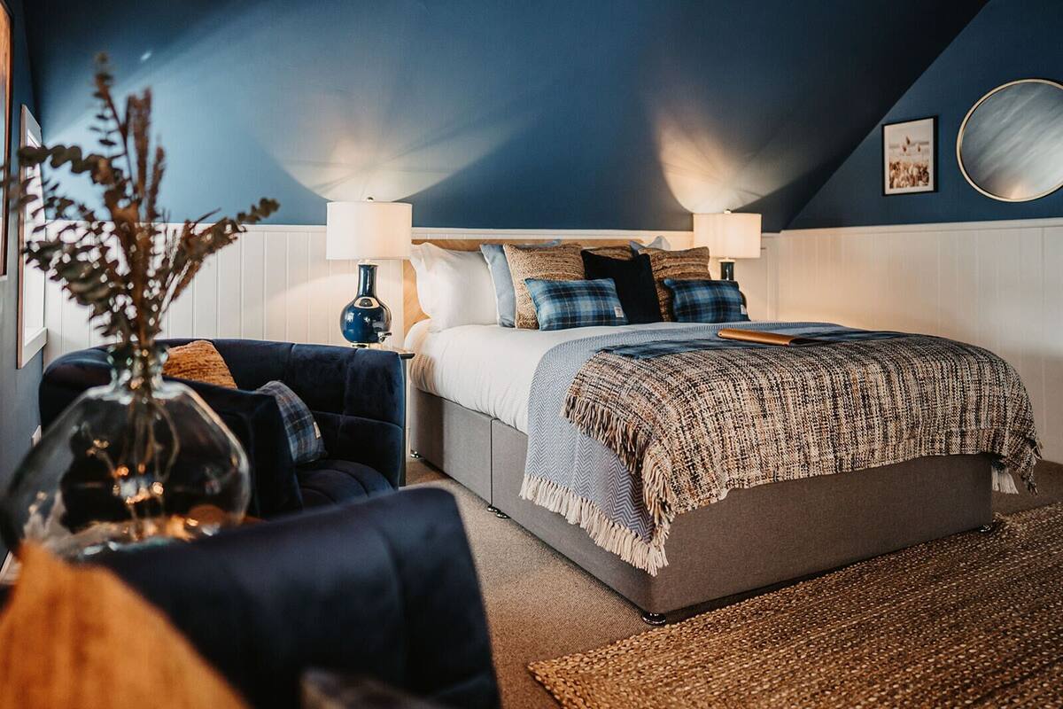 Quarto com cama, mesas de cabeceira, abajur, cadeira e um vaso decorativo.