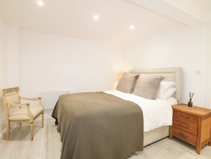 Um quarto com cama, mesa de cabeceira, cadeira e luminária na parede.