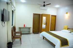 Quarto de hotel com cama, escrivaninha, cadeira, televisão e ventoinha no teto.