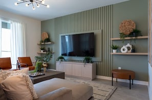 Uma sala de estar moderna com uma grande TV de tela plana, um sofá, uma mesa de centro e plantas decorativas.
