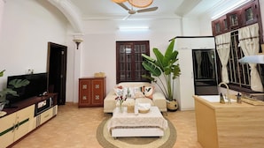 Uma sala de estar com sofá, televisão, plantas decorativas e ventilador de teto.