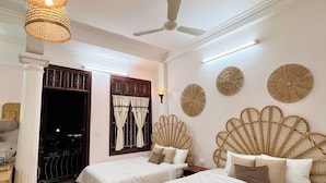 Quarto de hotel com duas camas, um ventilador de teto, luminária de fibra natural e decoração nas paredes.