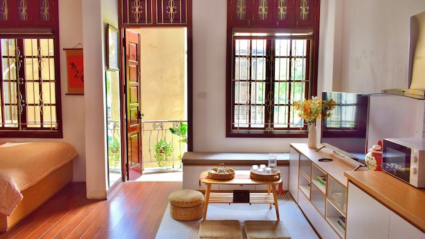 Quarto com uma cama, televisão, mesinha com objetos e vista para o exterior.