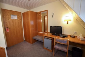Um quarto pequeno com uma escrivaninha, televisão, mini-geladeira e uma cadeira.