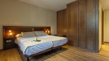 Quarto com cama grande, guarda-roupa de madeira, mesas de cabeceira com luminárias e um criado-mudo.