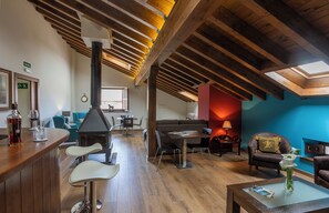 Um quarto espaçoso com teto alto, vigas de madeira, lareira, área de jantar e sala de estar com sofá e poltronas.