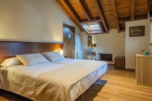 Quarto com cama grande, vigas de madeira no teto, claraboia, escrivaninha e uma cadeira.