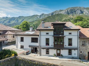 Um edifício de dois andares com telhado de telhas, janelas amplas e uma varanda com plantas em vasos.