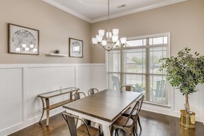 Uma sala de jantar com mesa de madeira, cadeiras, um lustre e um vaso de planta.