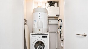 Uma lavanderia compacta com máquina de lavar frontal, secadora empilhada e aquecedor de água.