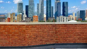Linha do horizonte de uma cidade com arranha-céus modernos, um muro de tijolos em primeiro plano e um céu azul límpido.