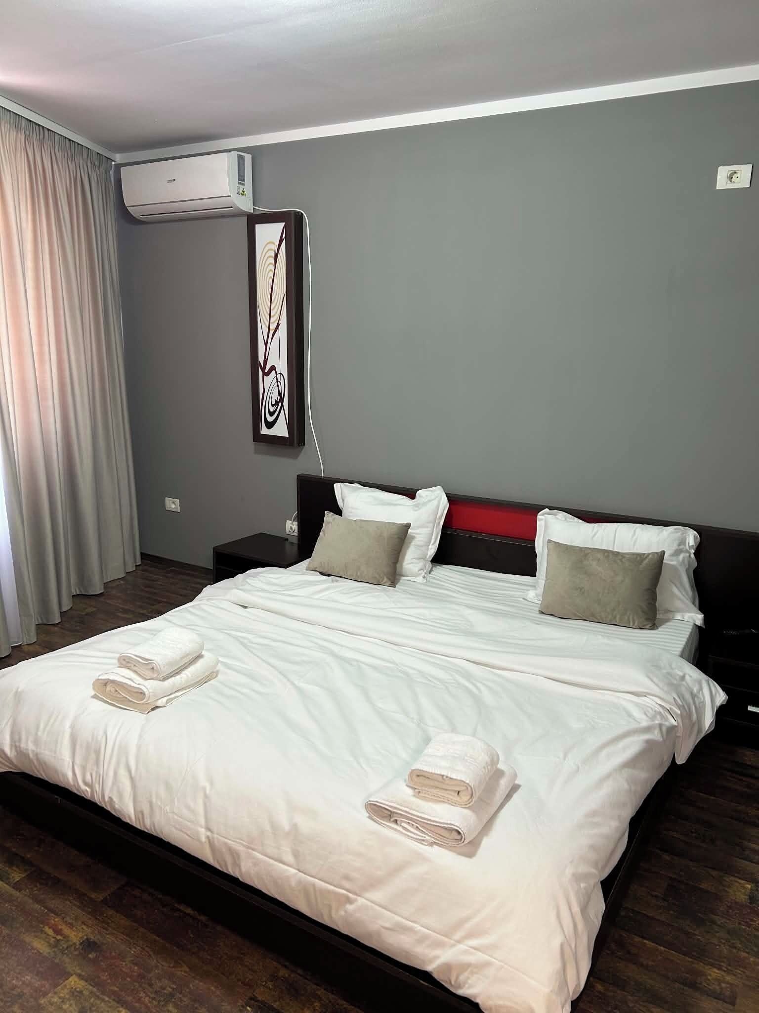 Quarto de hotel com uma cama grande, uma mesa de cabeceira, unidade de ar condicionado e uma obra de arte na parede.