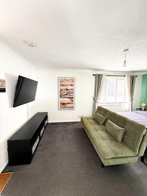 Quarto com sofá, televisão de tela plana, quadro na parede e janela com cortinas.