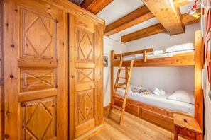 Uma cama beliche de madeira com escada, um guarda-roupa de madeira e um pequeno banquinho de madeira.