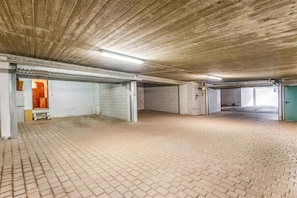 Garagem interna de estacionamento com piso de tijolos, paredes de concreto e teto de madeira.