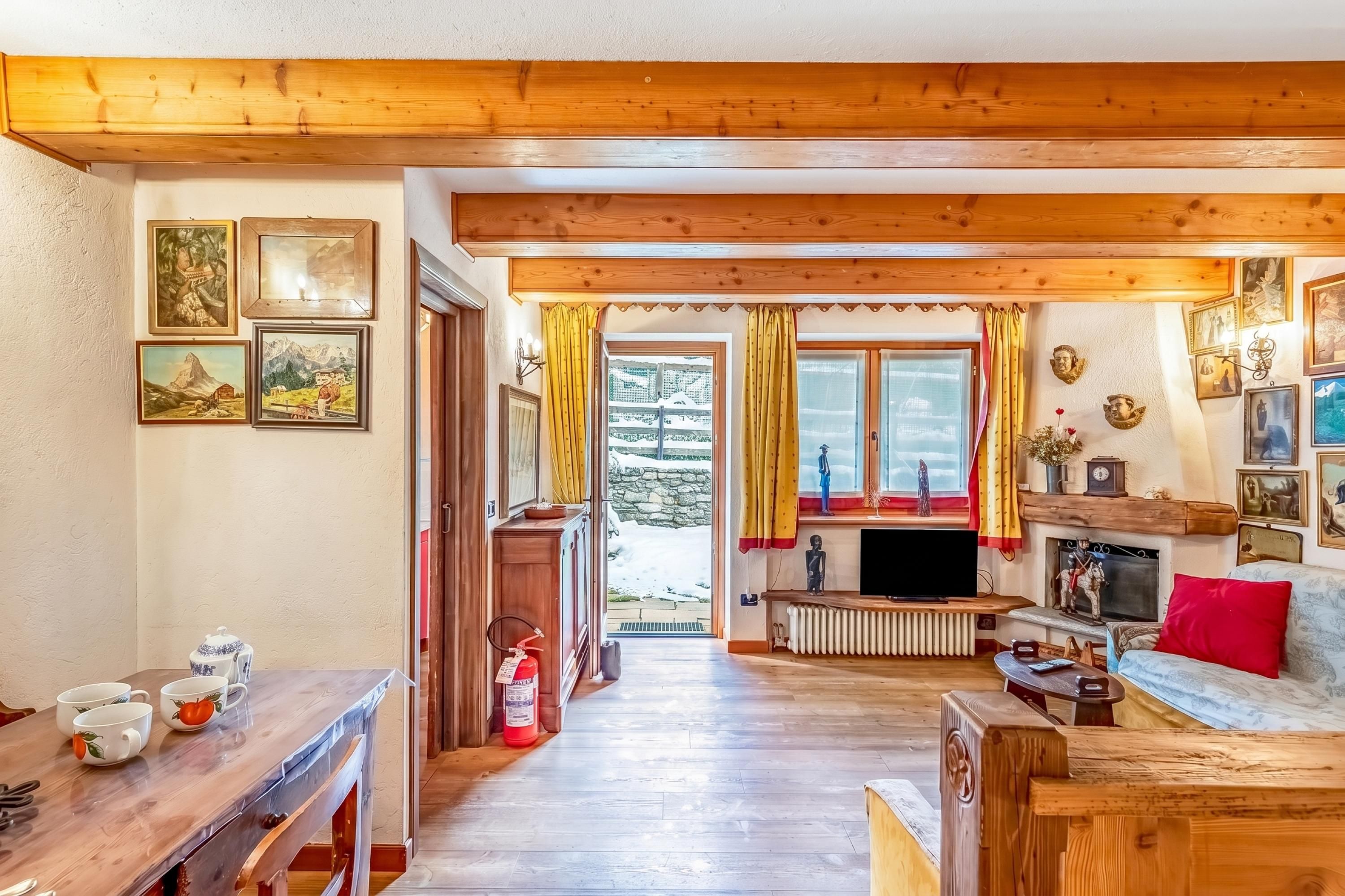 Uma sala de estar aconchegante com vigas de madeira, lareira e vista para uma paisagem coberta de neve.