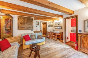 Uma sala de estar acolhedora com vigas de madeira, um sofá, uma mesa de centro e um espaço de jantar com um armário vermelho.