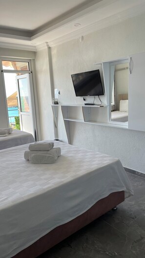Quarto de hotel com uma cama, televisão fixada na parede e janela com vista para o mar.