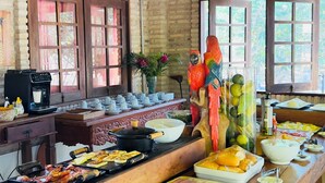 Disposição de buffet com diversos alimentos, uma máquina de café e elementos decorativos como uma escultura de papagaio.
