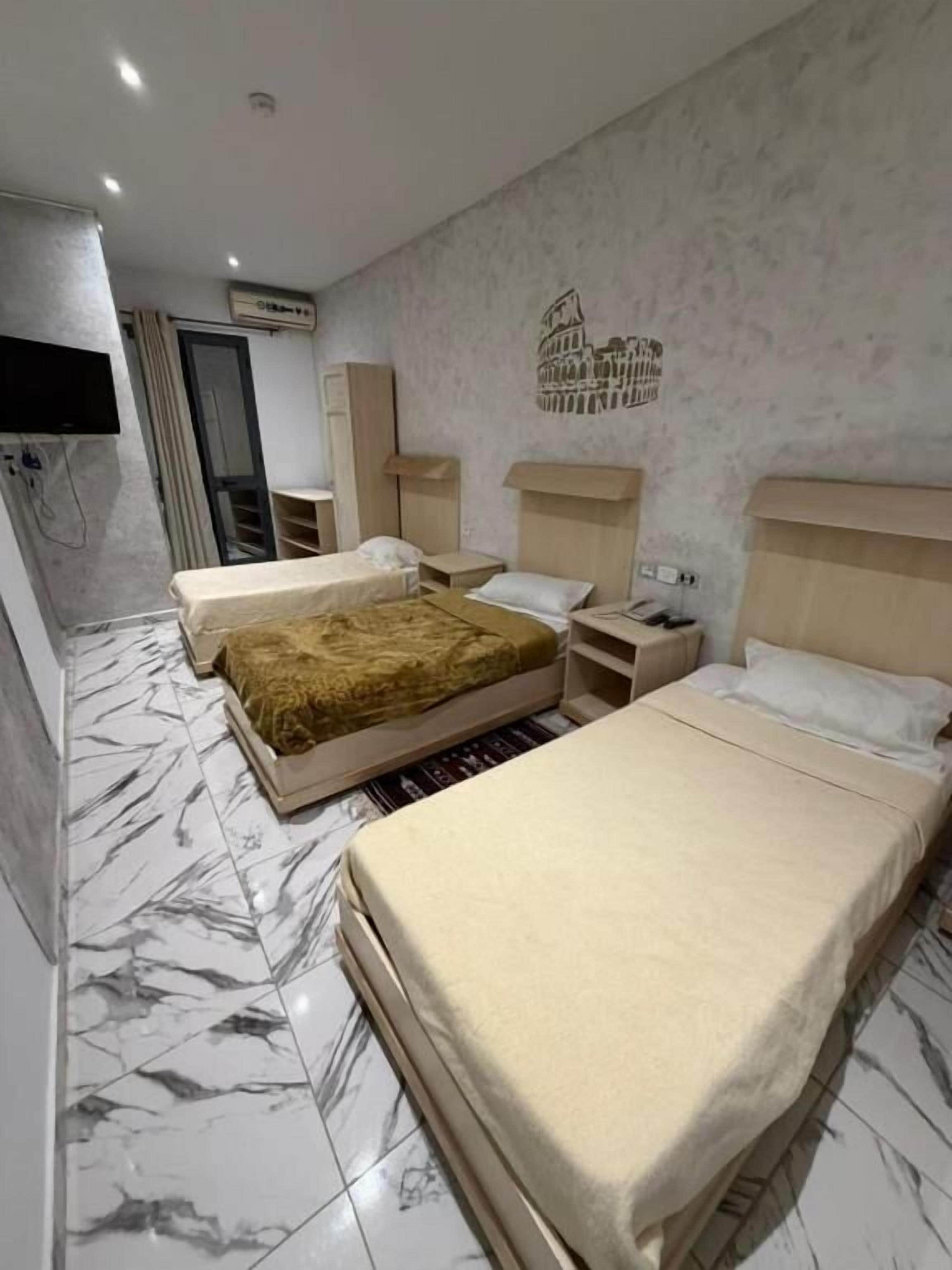 Quarto de hotel com uma cama grande, uma cama menor, uma televisão, um guarda-roupa e chão de mármore.
