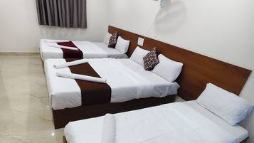 Quarto de hotel com três camas, um ventilador de teto e uma janela com cortinas.