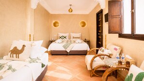 Quarto com cama, duas mesas de cabeceira, uma cadeira, uma mesinha com garrafas e televisão na parede.
