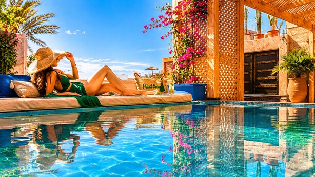 Área de piscina com uma pessoa relaxando, cerca de madeira e plantas em vasos.