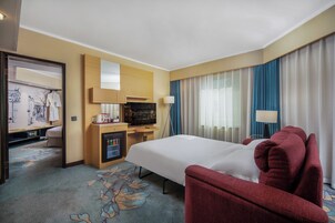 Quarto de hotel com uma cama, uma escrivaninha com computador, televisão e minibar.