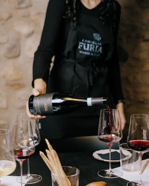 Alguém servindo vinho em copos sobre uma mesa, com parede de pedra ao fundo.