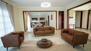 Uma sala de estar ampla com um sofá de couro marrom, uma mesa de centro de vidro e uma área de jantar ao fundo.