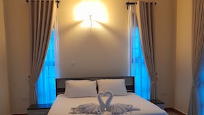 Quarto de hotel com cama, cortinas, luminária fixada na parede e mesa de cabeceira.