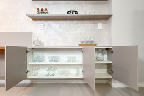 Cozinha com armários abertos exibindo copos e uma prateleira com objetos decorativos.