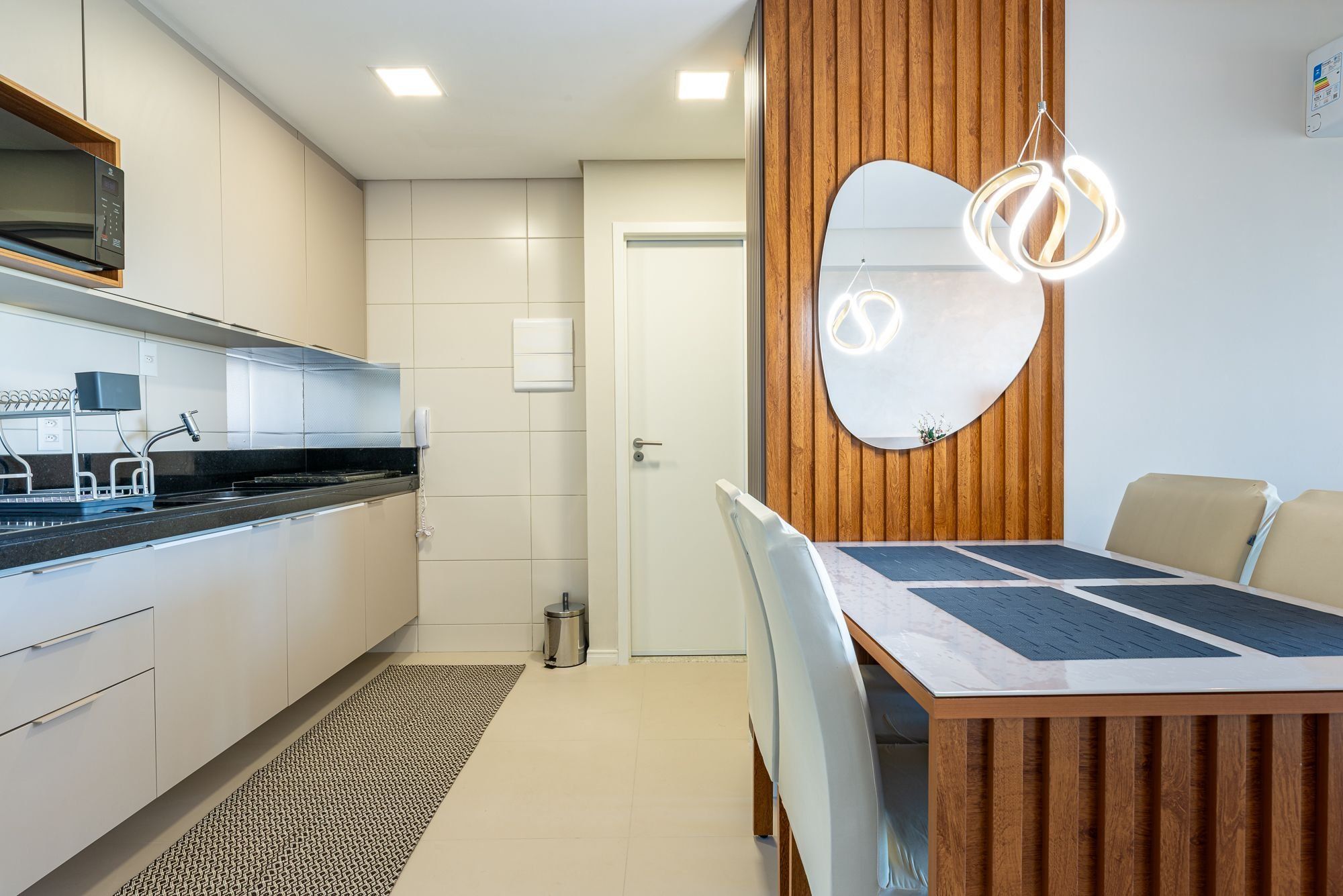 Cozinha moderna com micro-ondas embutido, pia e área de jantar com mesa e cadeiras de madeira.