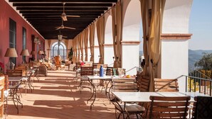Um pátio ao ar livre com mesas e cadeiras de madeira, um longo banco e vista para as montanhas.