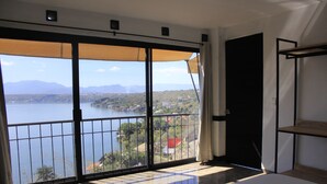 Quarto com uma grande janela com vista para um corpo de água e paisagem montanhosa.