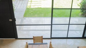 Espaço de estar integrado com mesa de jantar, cadeiras e vista para área externa por grandes portas de vidro.
