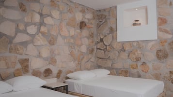Quarto com parede de pedra, duas camas, uma mesa de cabeceira e um quadro pendurado na parede.
