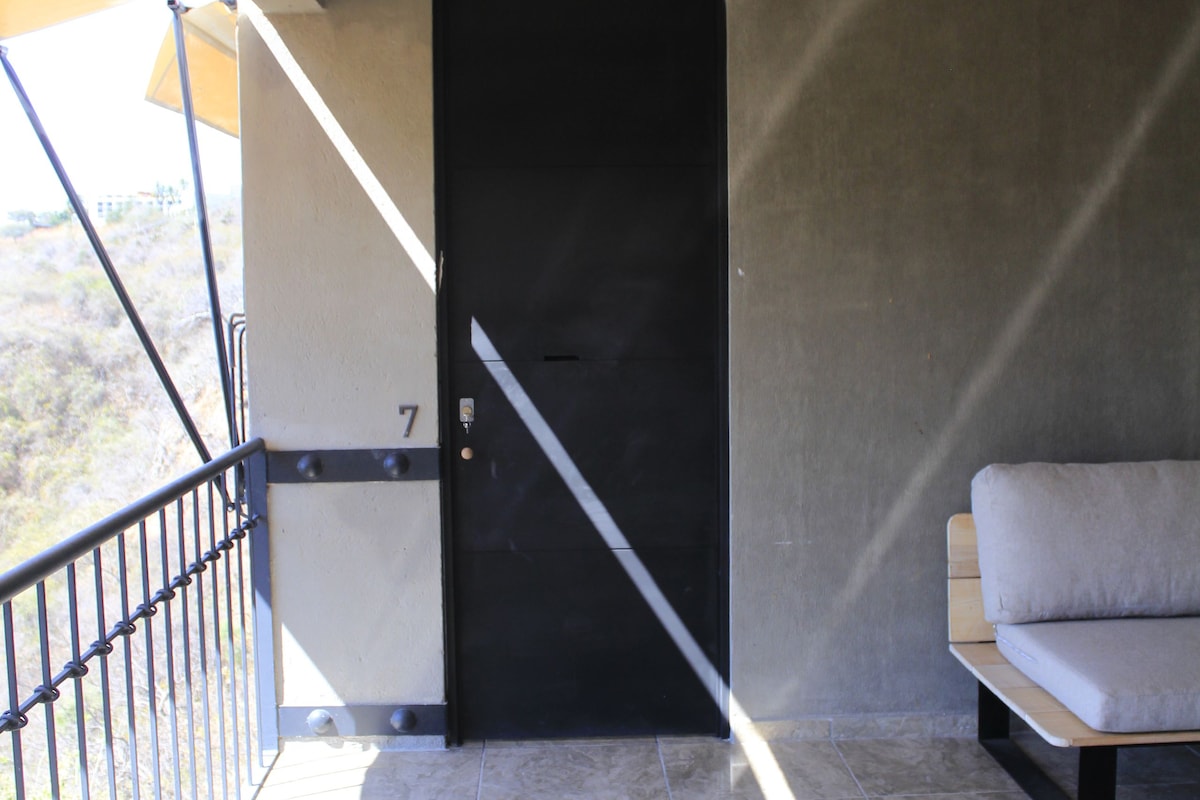 Uma varanda com grades de metal, uma porta preta e um sofá bege.