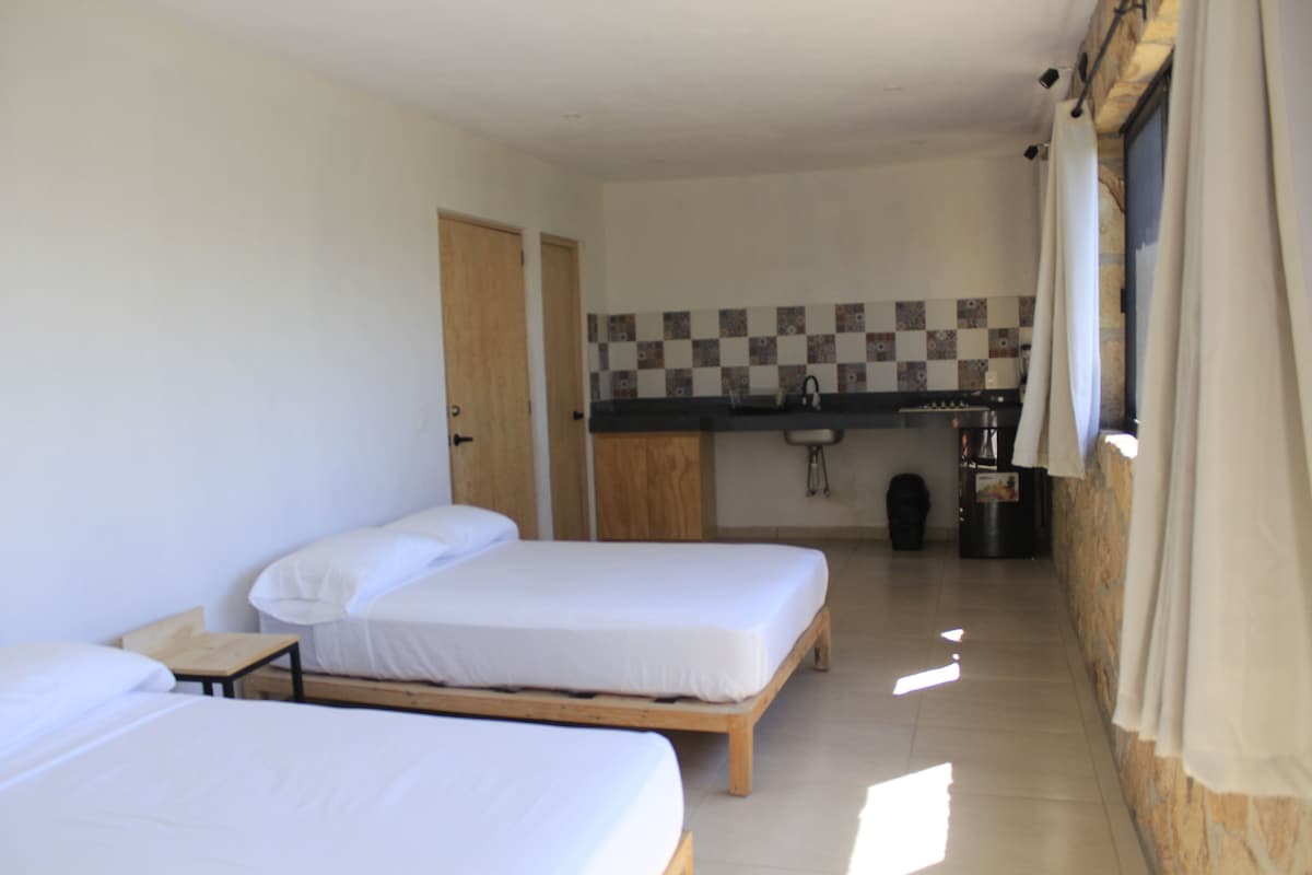 Quarto com duas camas, um kitchenette e um banheiro.