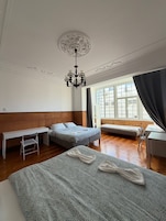 Quarto de hotel com uma cama grande, uma escrivaninha, uma cadeira, uma mesa pequena e uma janela com cortinas.