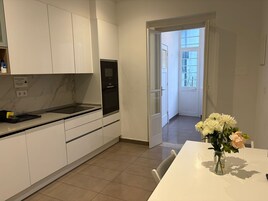 Uma cozinha moderna com armários brancos, forno embutido e um espaço de jantar com mesa e vaso de flores.