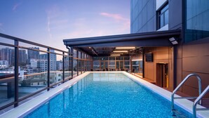 Piscina no terraço com barreira de vidro, cercada por um edifício moderno com amplas janelas.