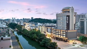 Um hotel moderno com uma torre imponente, um rio ao lado e um cenário de colinas ao fundo.